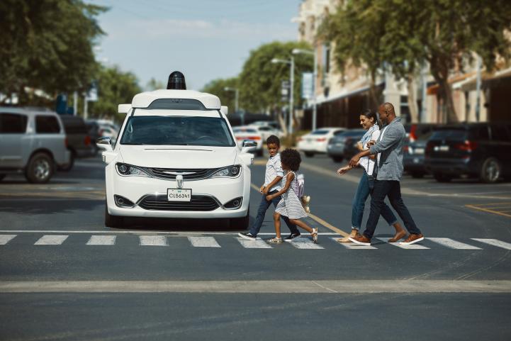 Waymo vehicle in a downtown setting with pedestrians crossing the street