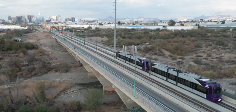 A light rail train crosses a bridge with the Phoenix skyline in the ...